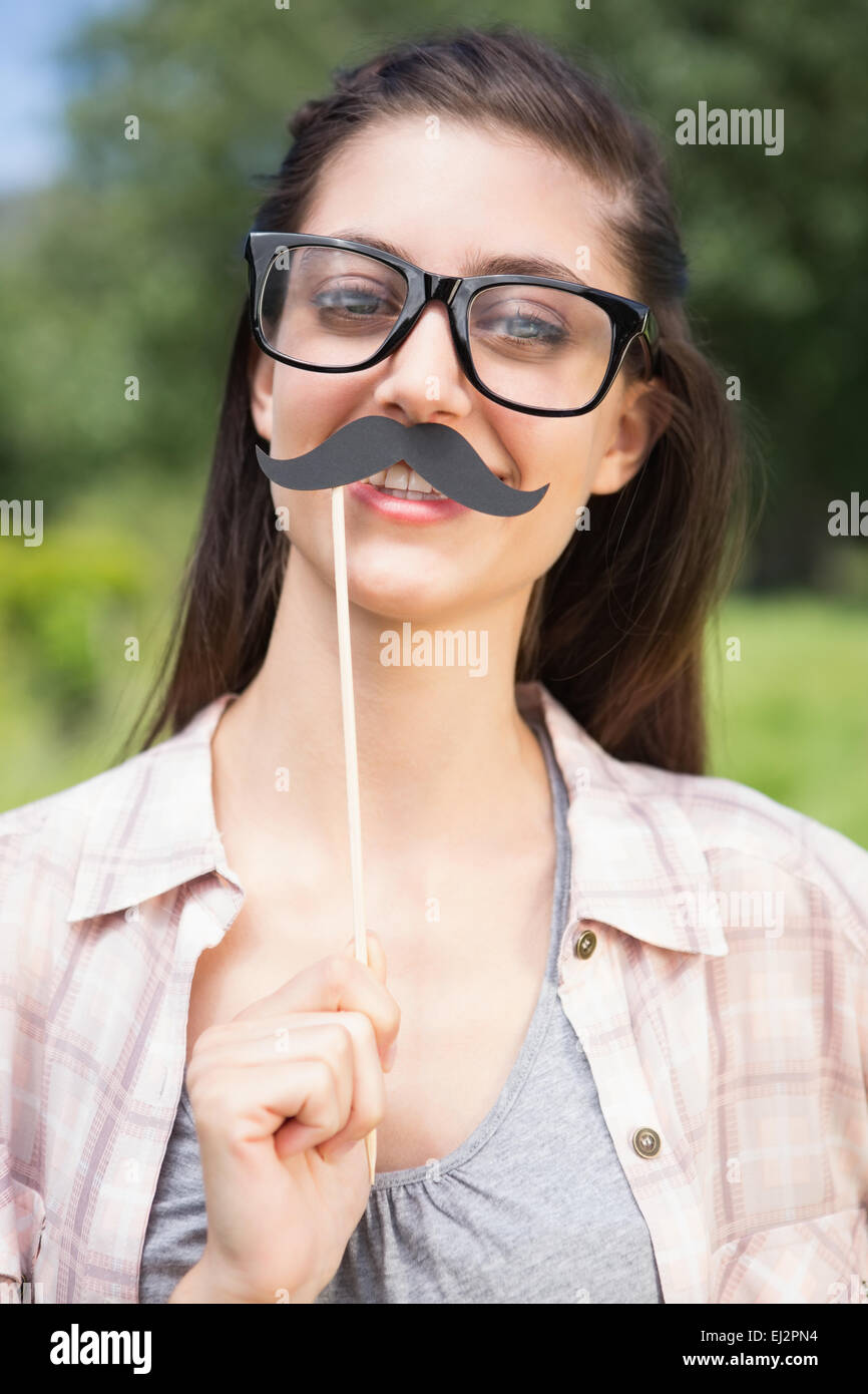 Pretty brunette smiling at camera with fake mustache Stock Photo - Alamy
