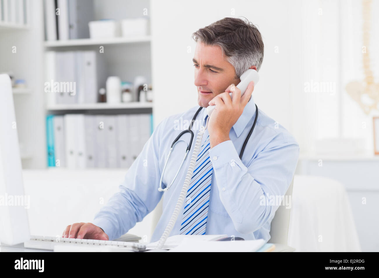 Doctor using telephone while working on computer Stock Photo - Alamy