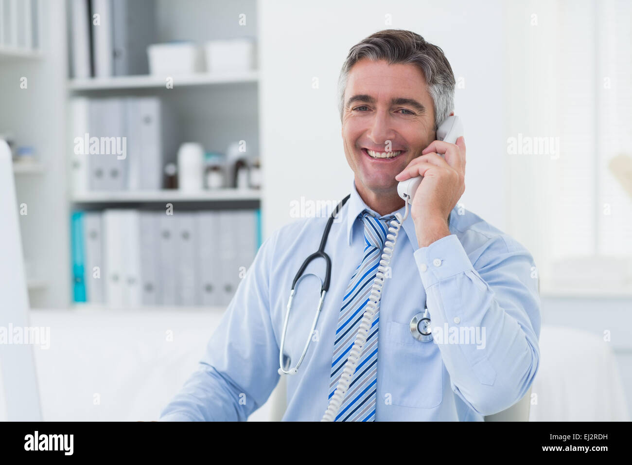 Confident male doctor using telephone in clinic Stock Photo - Alamy