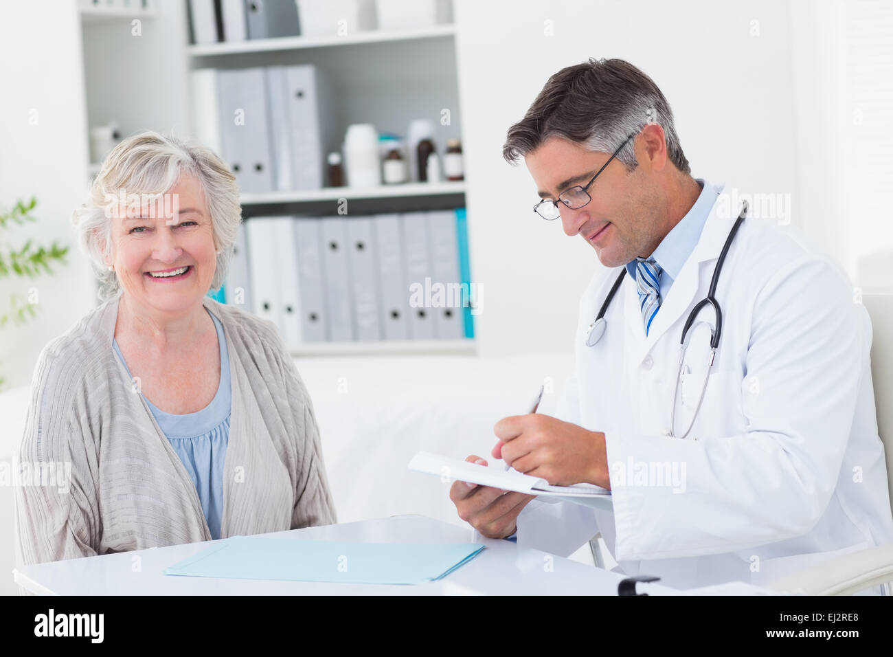 Doctor writing prescription while female patient smiling Stock Photo ... Doctor writing prescription while female patient smiling Stock Photo ...