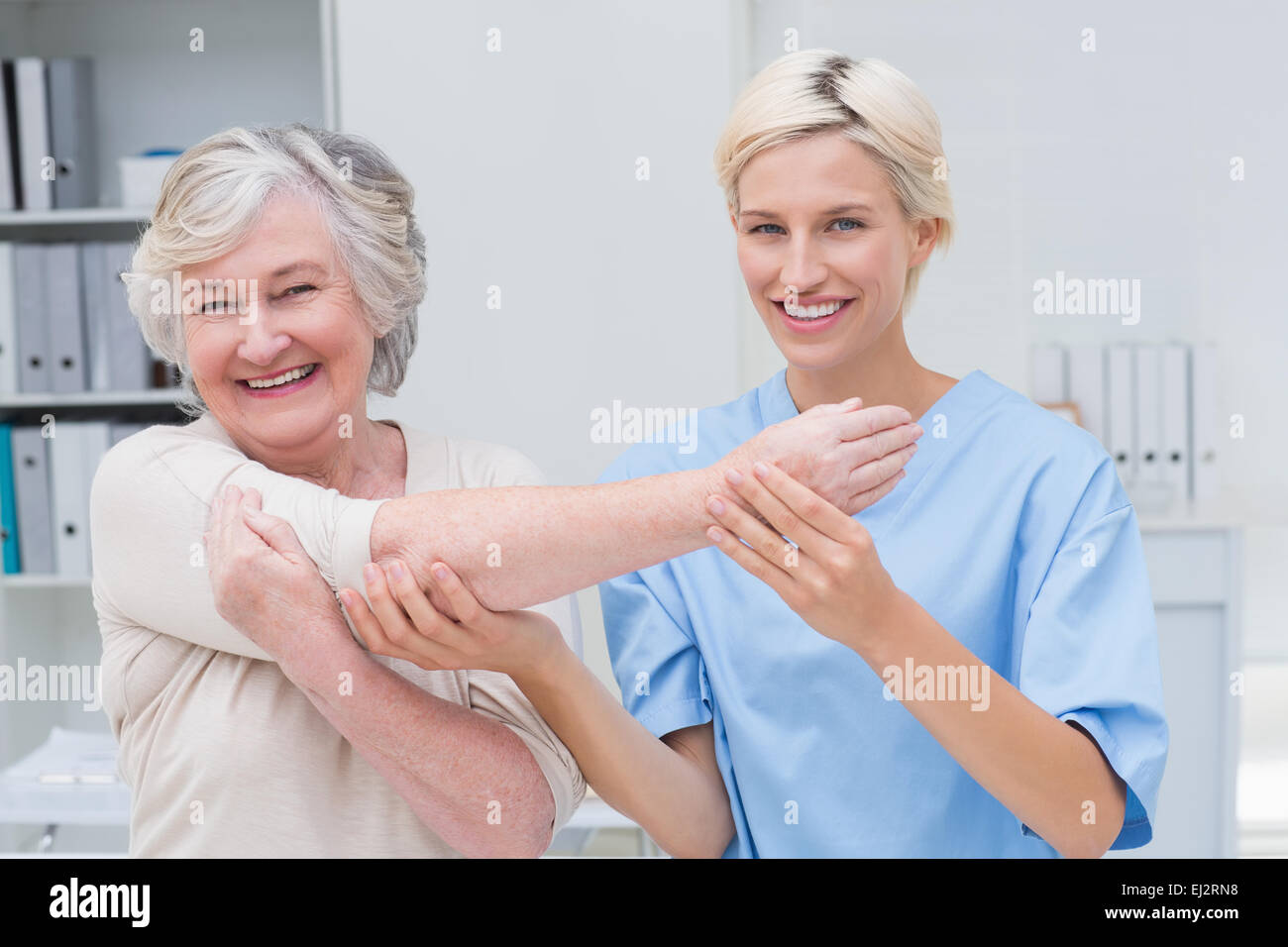 Smiling nurse assisting senior patient in raising arm Stock Photo - Alamy