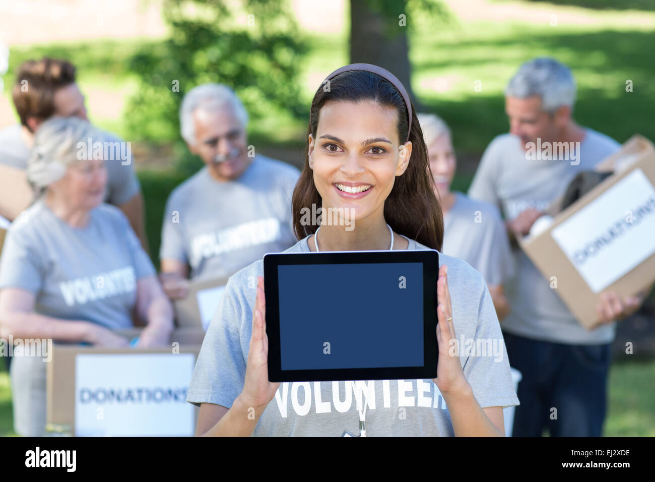 Smiling volunteer brunette showing tablet pc screen Stock Photo - Alamy