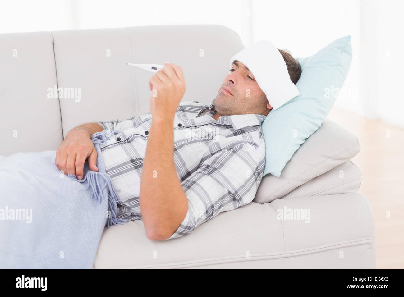Ill man checking temperature on thermometer Stock Photo - Alamy