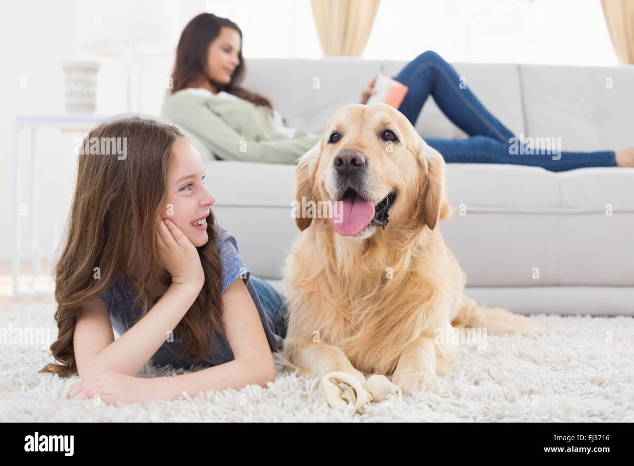 Girl looking at dog while lying on rug Stock Photo - Alamy