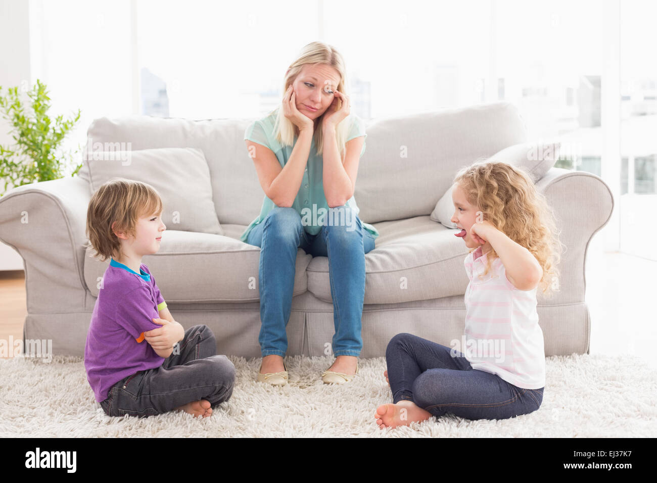 Upset mother looking at children fighting on rug Stock Photo - Alamy