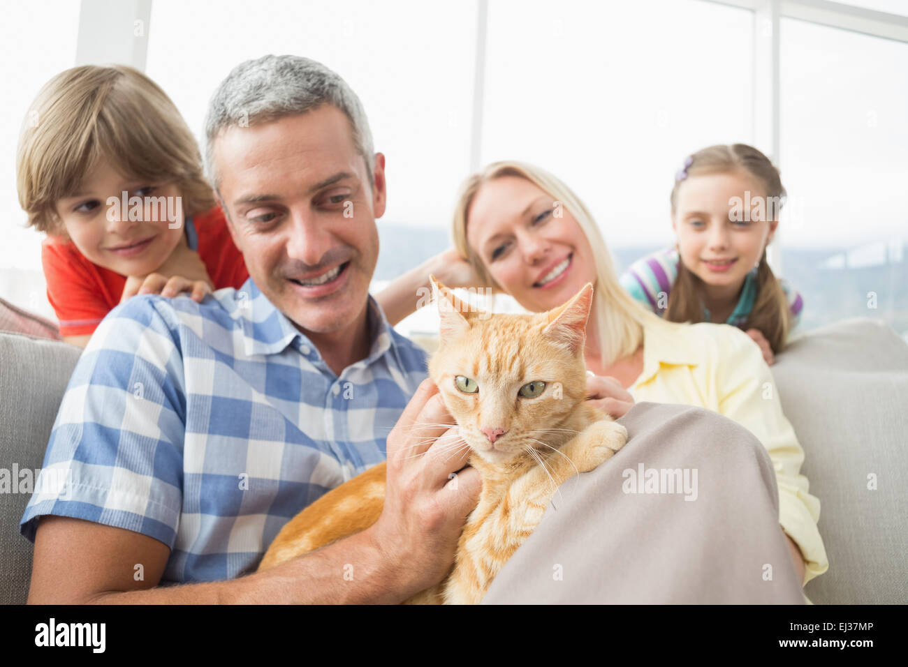 Family sitting with cat on sofa at home Stock Photo - Alamy