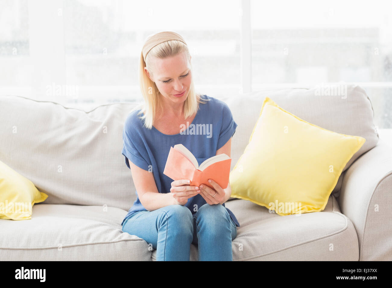Woman reading book on sofa Stock Photo - Alamy