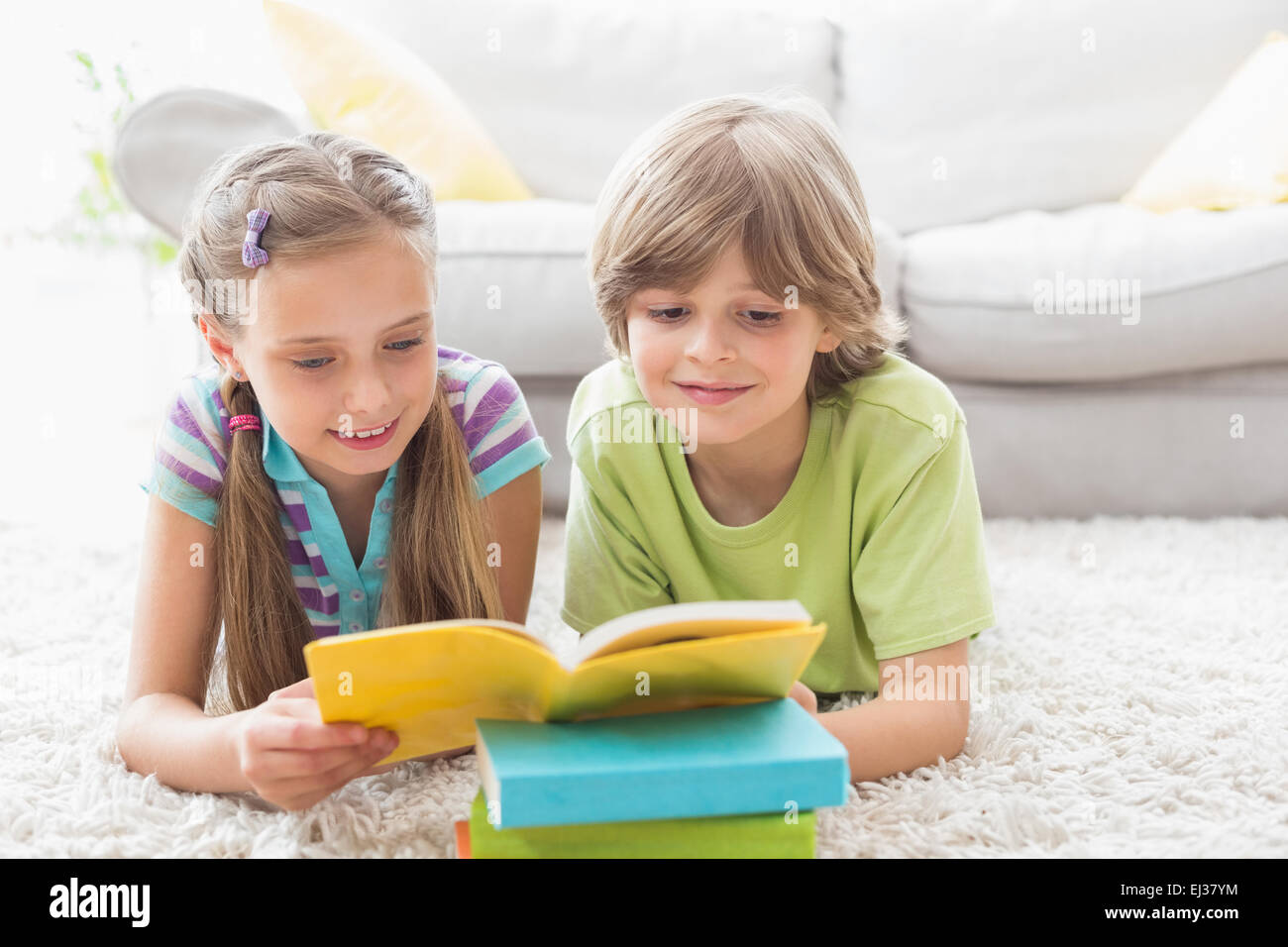 Siblings reading book while lying on rug Stock Photo - Alamy