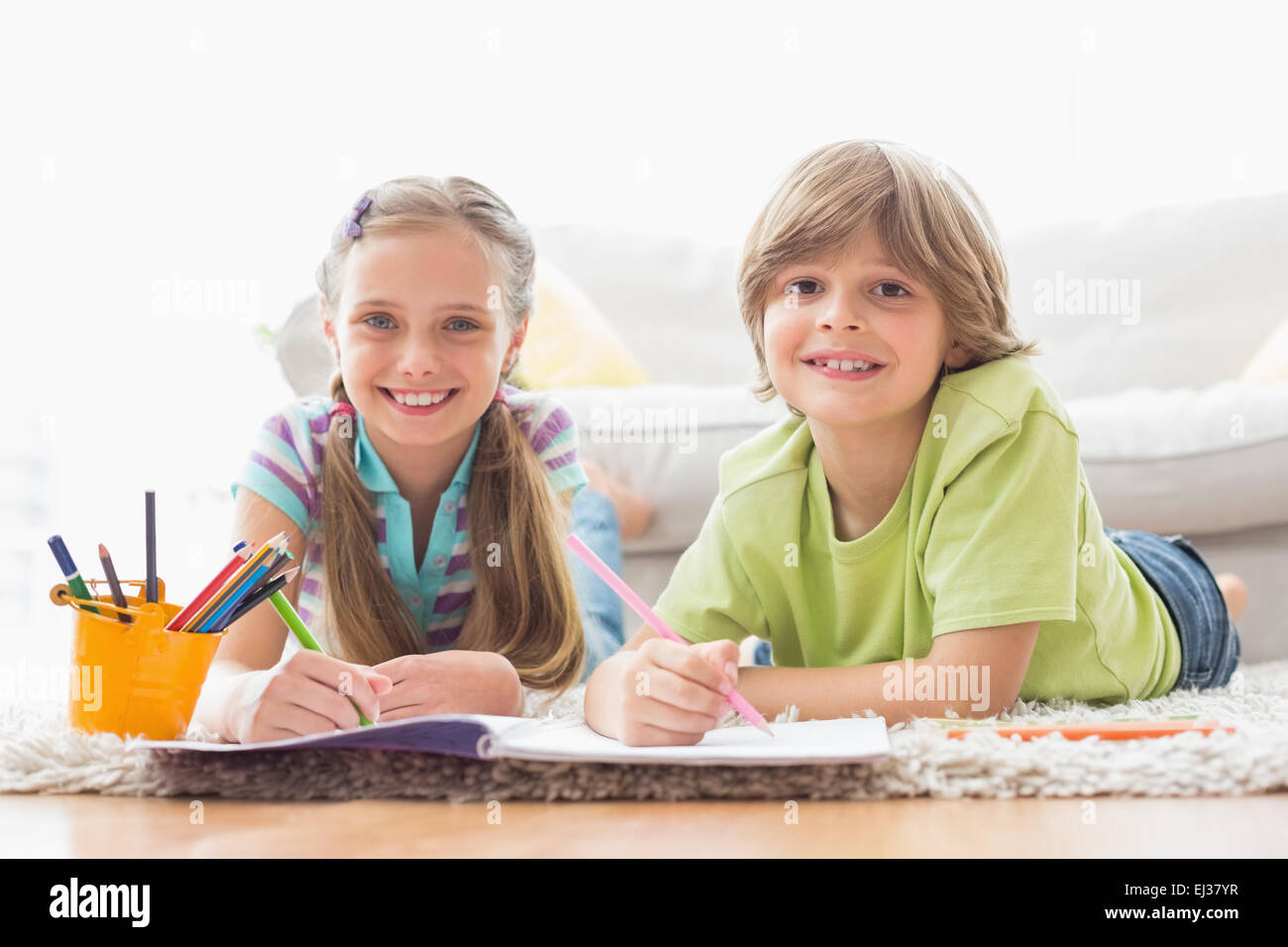 Portrait of happy siblings drawing while lying on rug Stock Photo - Alamy