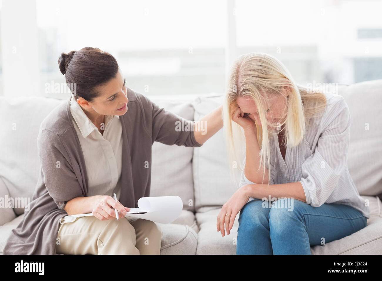 Therapist comforting upset woman on sofa Stock Photo - Alamy