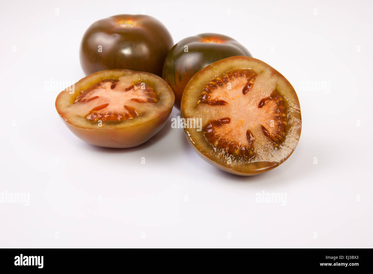 Dark green kumato tomatoes, whole and sliced. Isolated over white ...