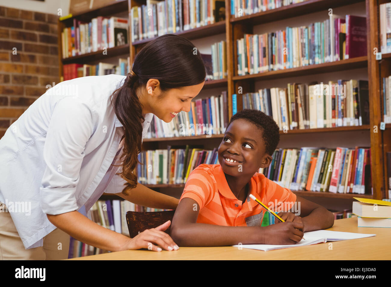 Teacher assisting boy with homework in library Stock Photo - Alamy