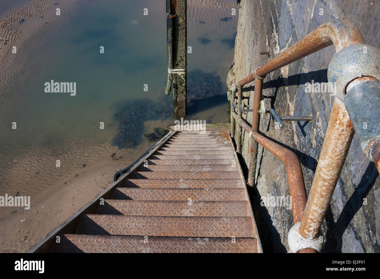 seaside old rusting steel steps with handrail fixed to jetty wall ...