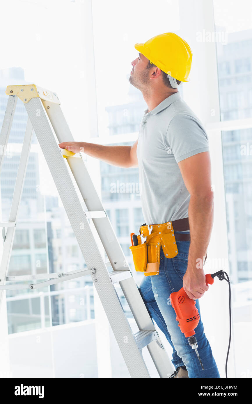 Handyman with drill machine climbing ladder in building Stock Photo - Alamy