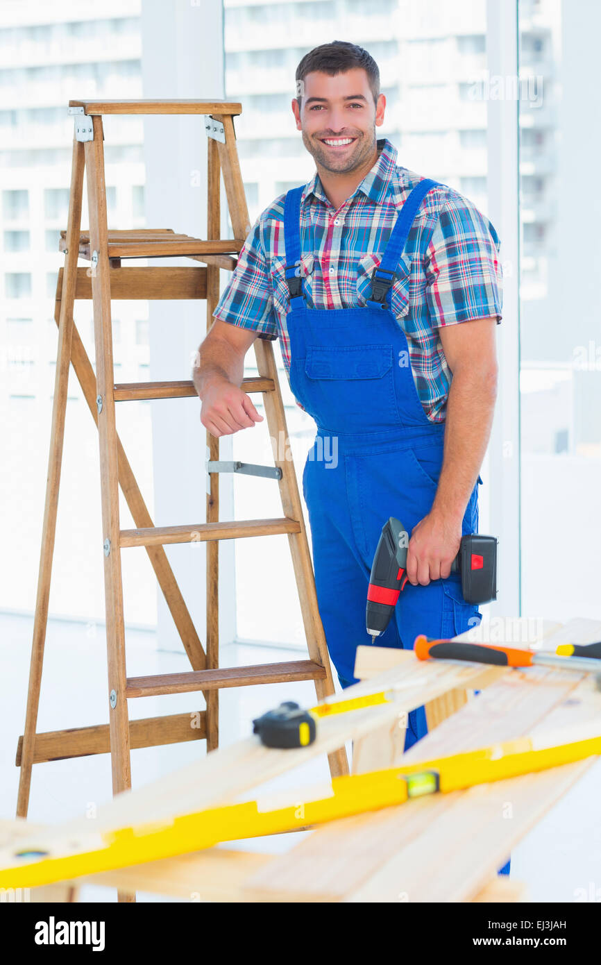 Carpenter with power drill standing by ladder at construction site ...