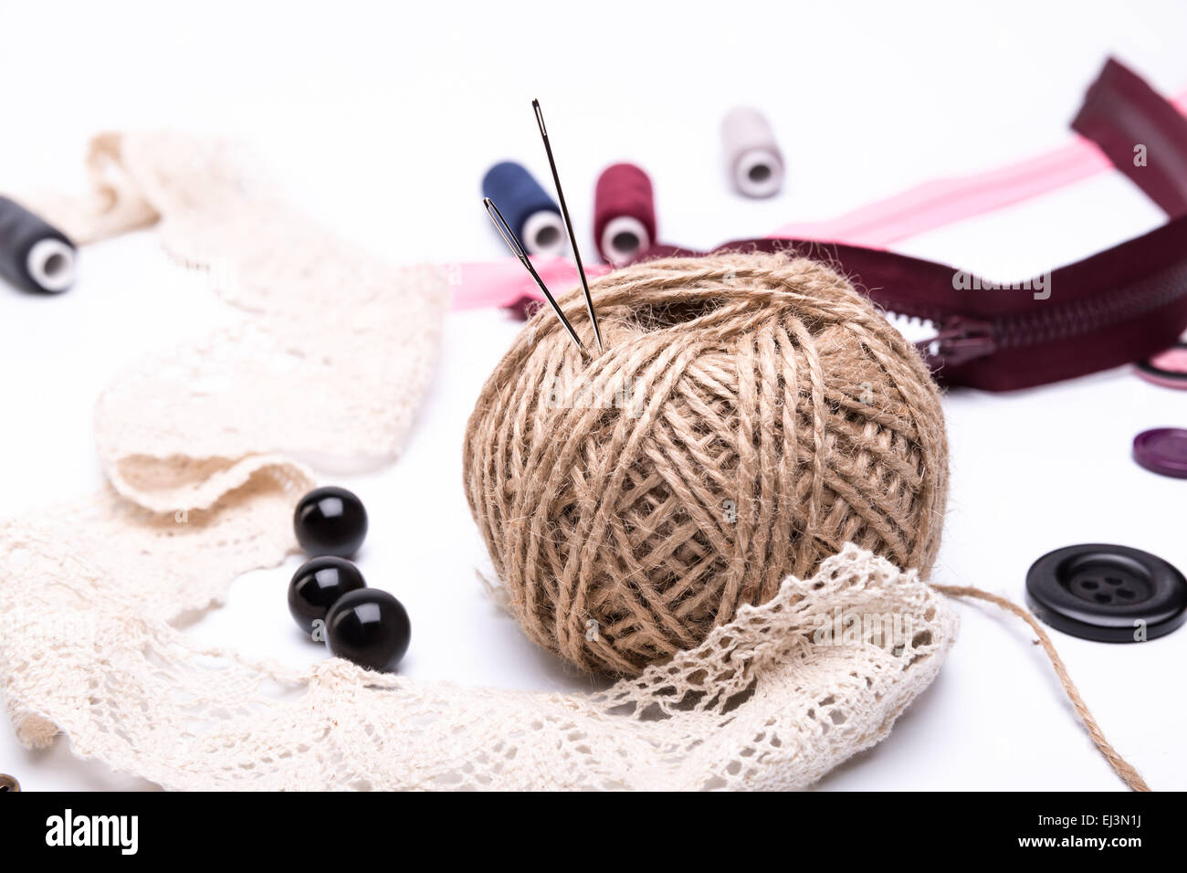 bunch of various sewing accessories and a needle stuck into the skein of thread on a white ...