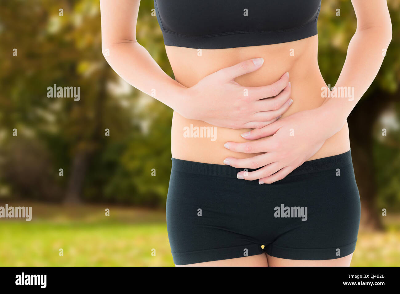Composite image of mid section of a fit young woman with stomach pain ...