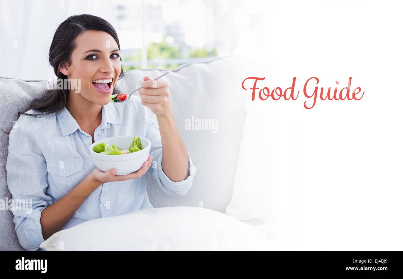 Food guide against cheerful woman relaxing on the sofa eating salad ...