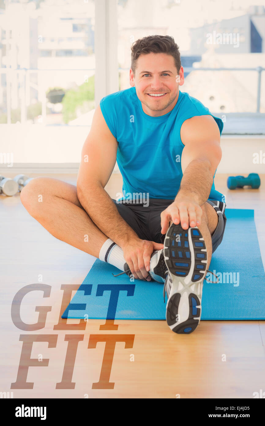 Composite image of sporty man stretching hand to leg in fitness studio ...