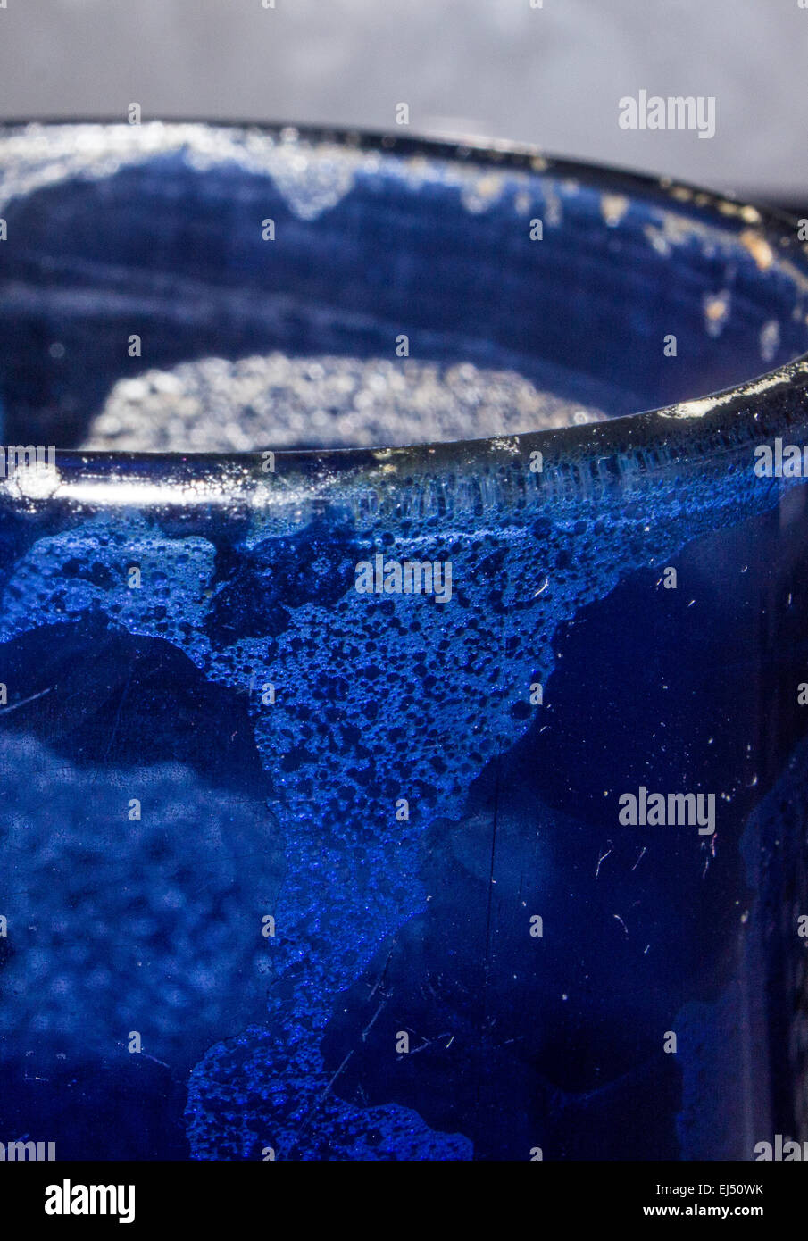A blue, see through coffee mug with froth from after drinking a ...
