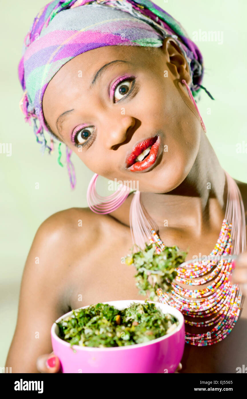 Young Kenyan woman with head scarf eating sukuma wiki in studio setting ...