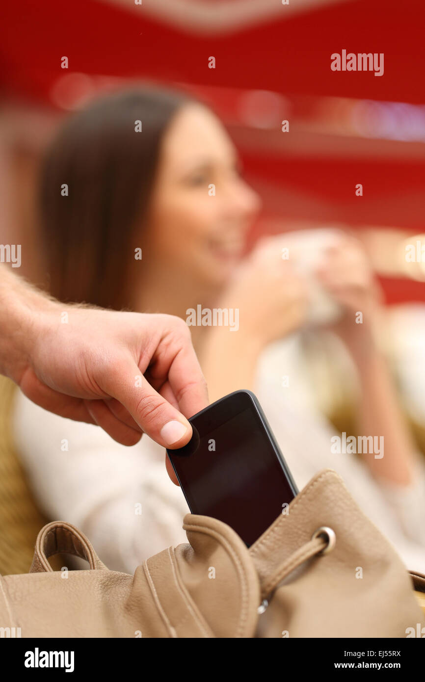 Thief hand stealing a mobile phone from a woman bag while she is ...