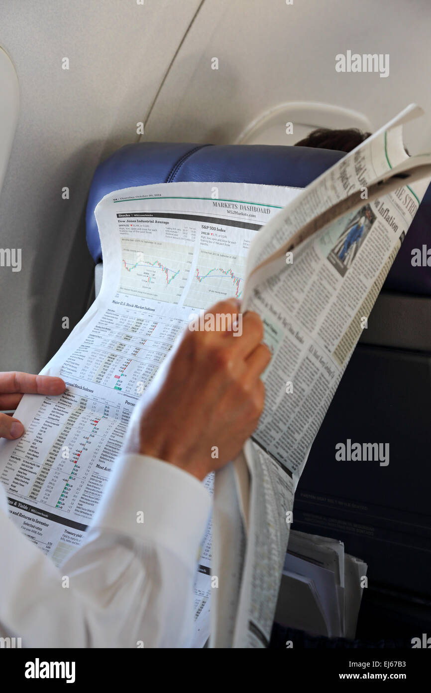 Passenger reads stock market page of newspaper on airplane in airplane ...