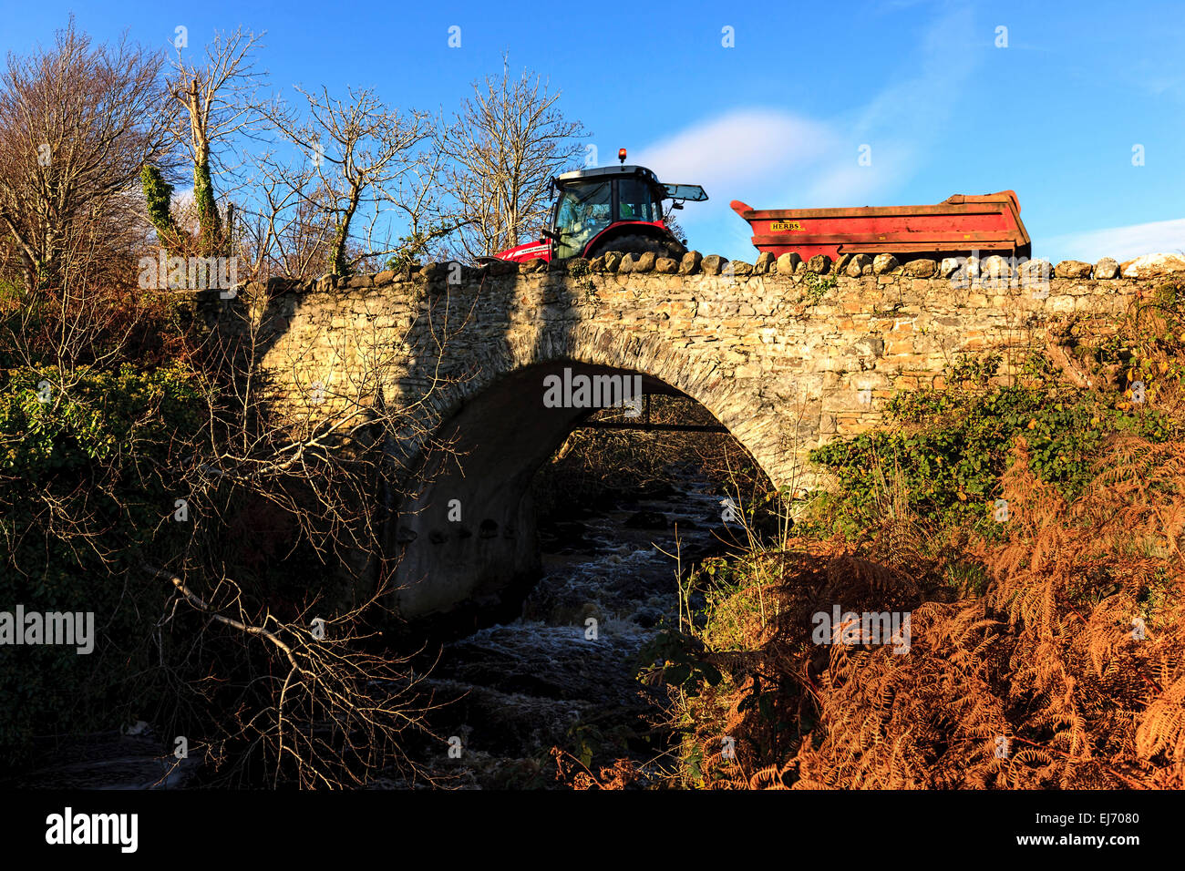 Tractor with trailer crossing over old stone bridge with water creek ...