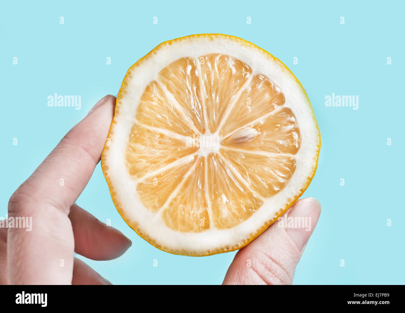 Sliced lemon on light blue background with fingers squeezing it Stock ...