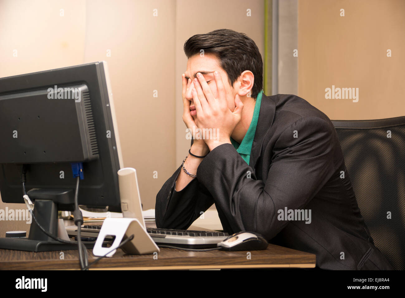 Tired bored young businessman sitting at his desk in front of his ...