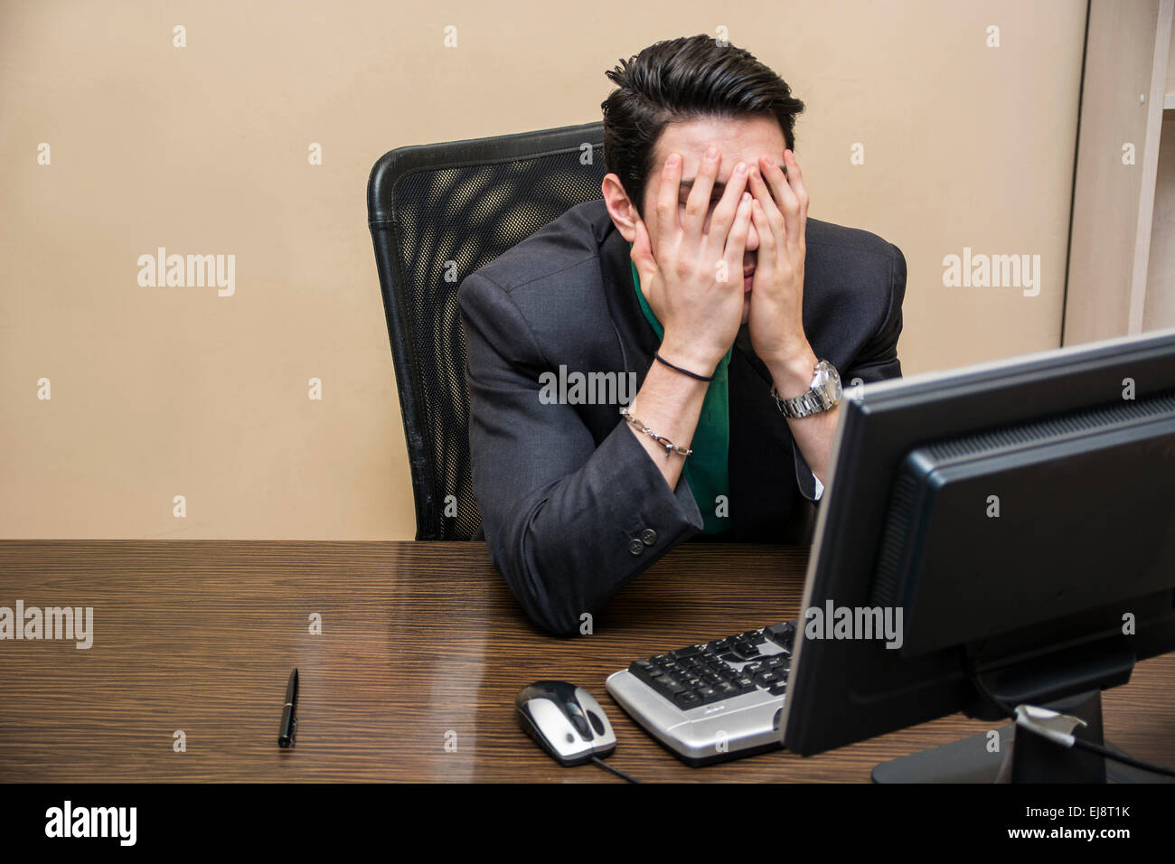 Desperate, worried young businessman sitting at his desk in front of ...