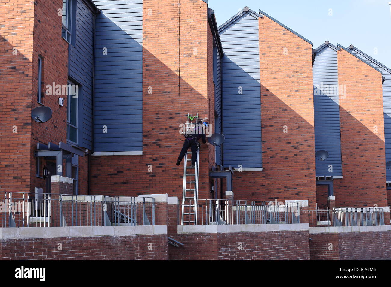 A workman up a ladder repairing a satellite dish on a property at ...