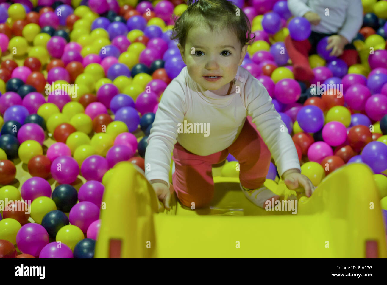 Little baby girl climbing the slide over colorful balls background ...