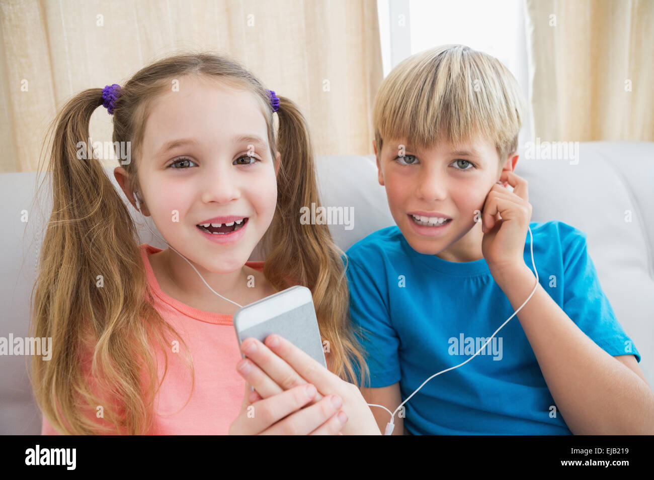 Happy siblings listening to music on sofa Stock Photo - Alamy