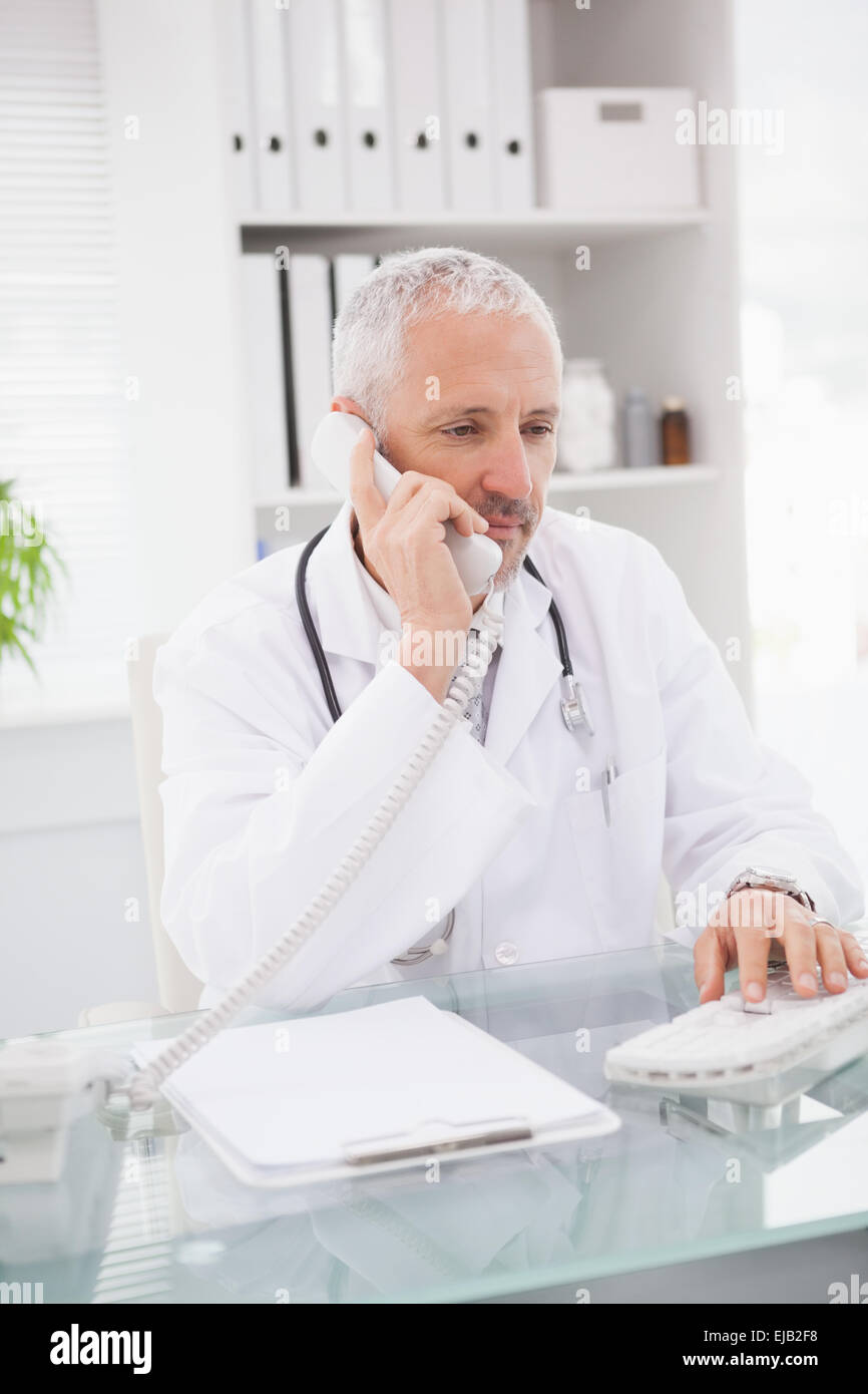 Doctor phoning and using computer Stock Photo - Alamy