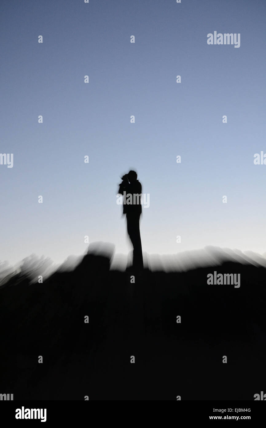 A Lone man standing on a mountain top looking out over the landscape ...