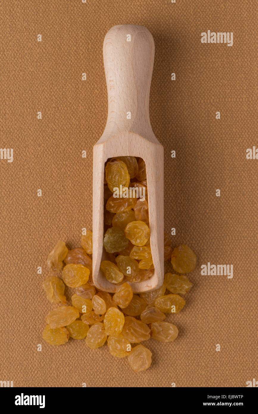 Top view of wooden scoop with golden raisins against brown vinyl ...