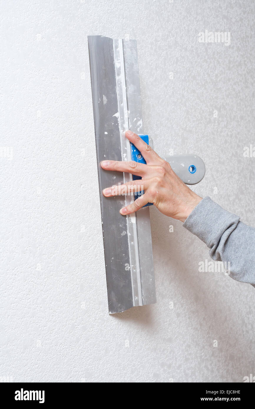 Human hand holding a large spatula and smoothes decorative plaster ...