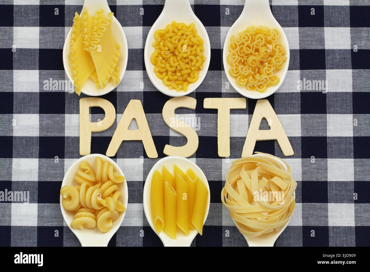 Pasta written with wooden letters on checkered cloth and uncooked pasta ...