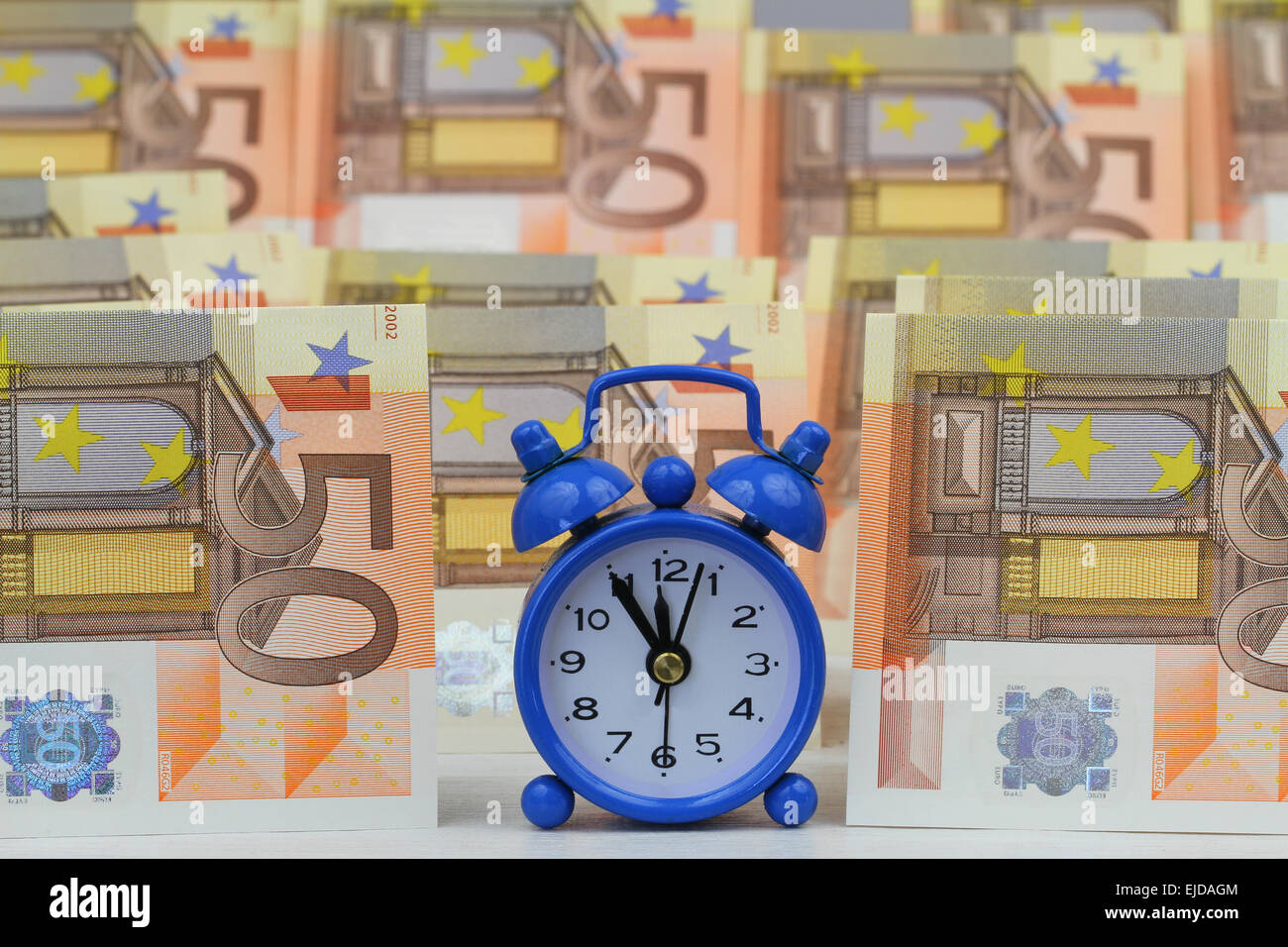 Miniature clock with banknotes in the background Stock Photo - Alamy