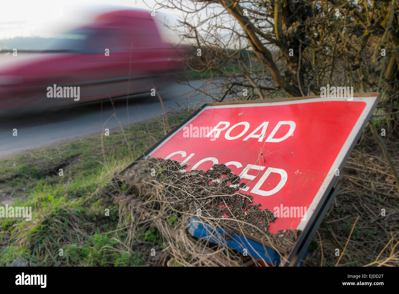 Road closed sign left at a roadside with a vehicle passing at speed ...
