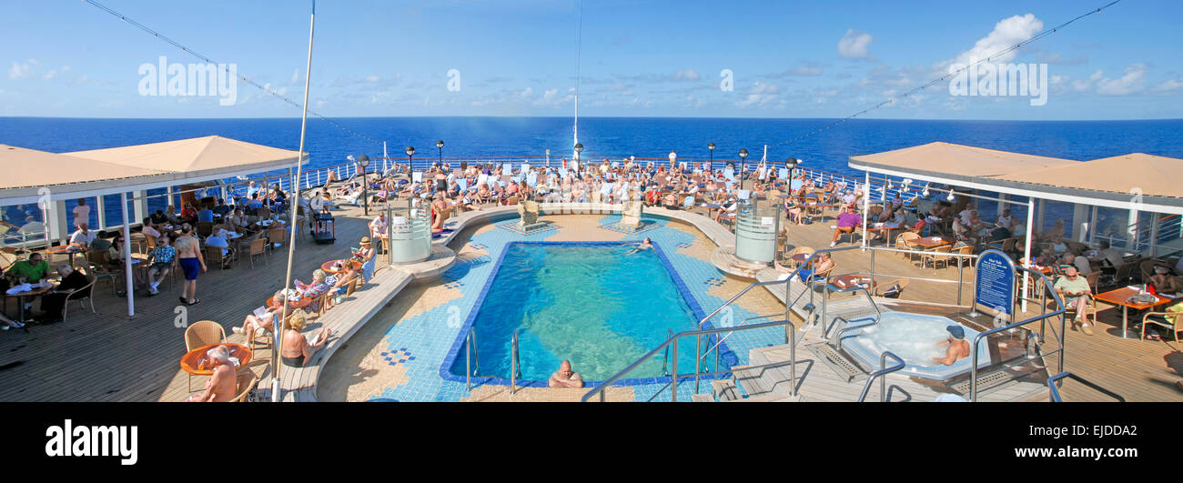 Panoramic view of passengers relaxing in the sun by the pool on cruise ...