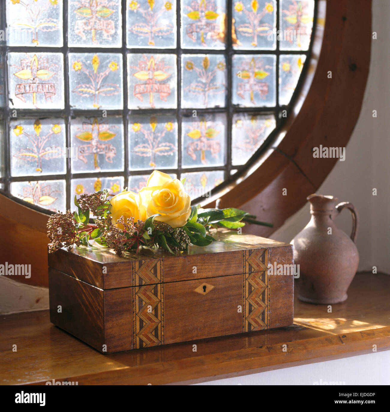 Yellow roses on an antique inlaid box below a circular stained glass ...