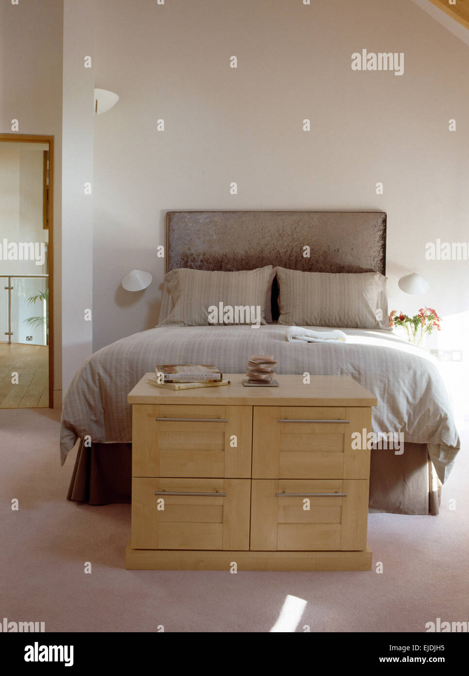 Pale wood chest below bed with upholstered headboard and pale gray ...