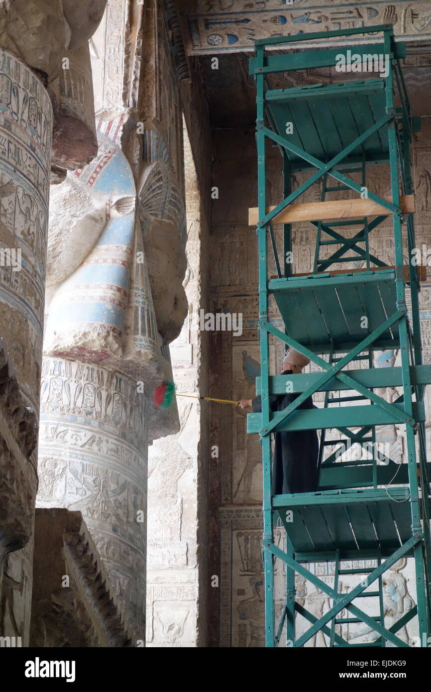 Workman on scaffold tower dusting giant capital at Denderah, Egypt ...