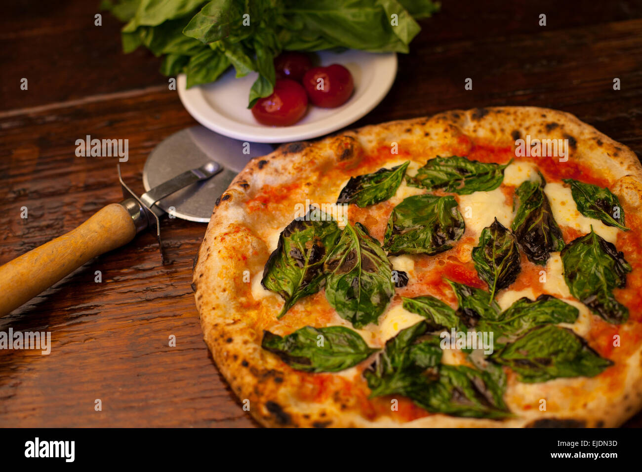 Uncut whole Basil Pizza with cutting wheel and ingredients on wooden ...