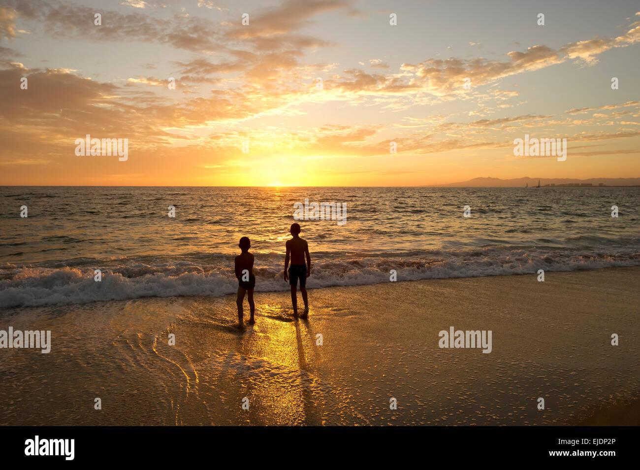 Two boys watch in awe as the sun sets on the water Stock Photo - Alamy
