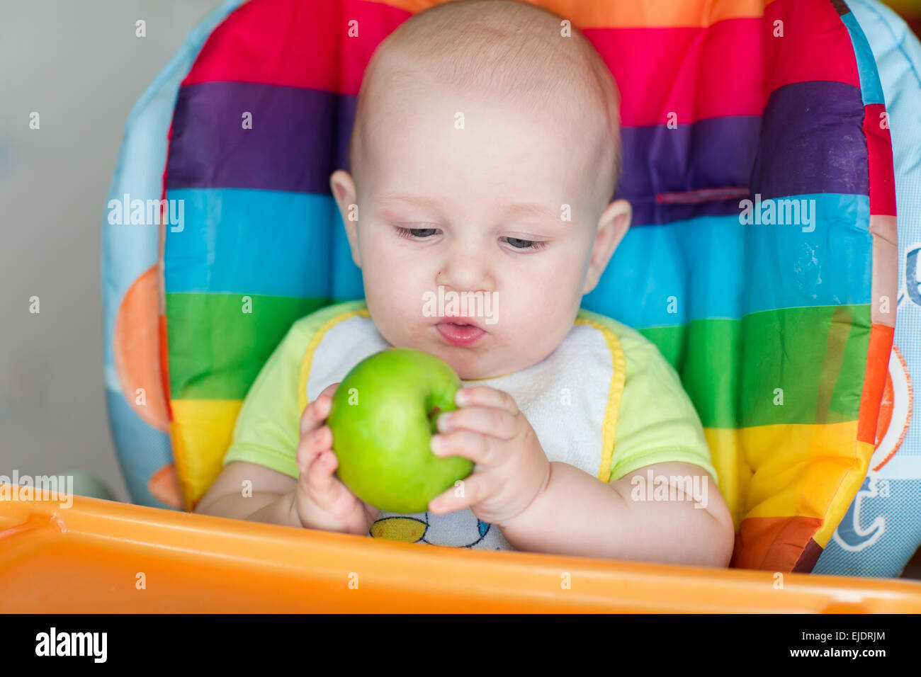 Adorable baby eating apple in high chair. Baby's first solid food Stock ...
