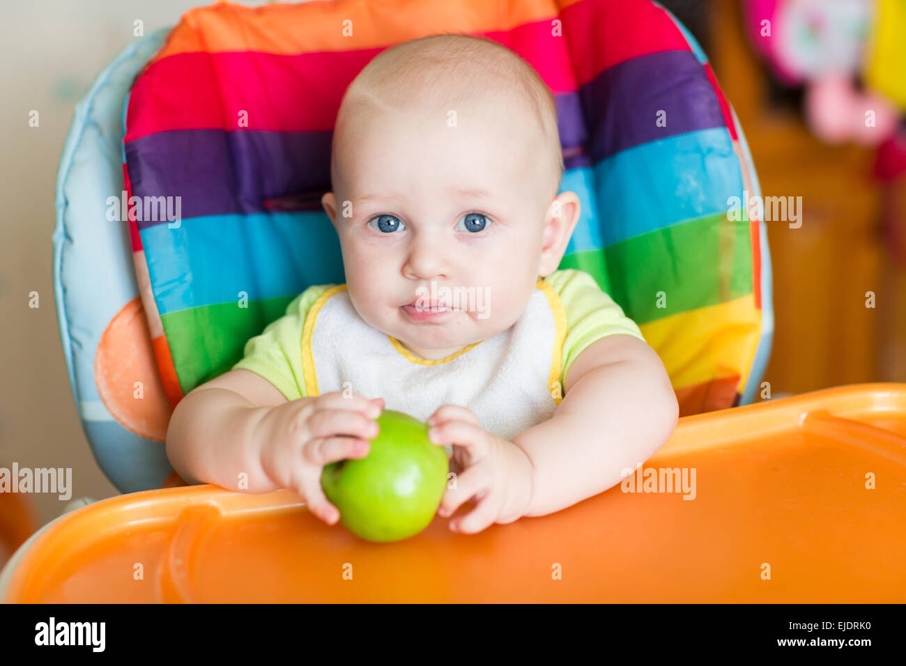 Adorable baby eating apple in high chair. Baby's first solid food Stock ...