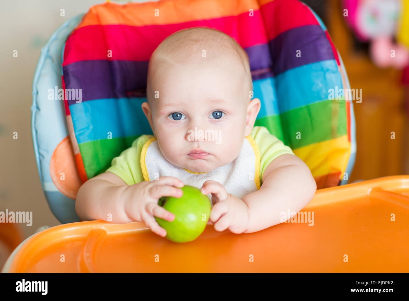 Adorable baby eating apple in high chair. Baby's first solid food Stock ...